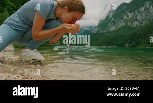 A person drinking fresh water and washing face with clear lake water ...