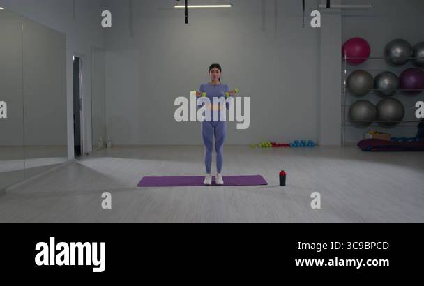 sporty girl stands in a modern gym confidently doing biceps exercises ...