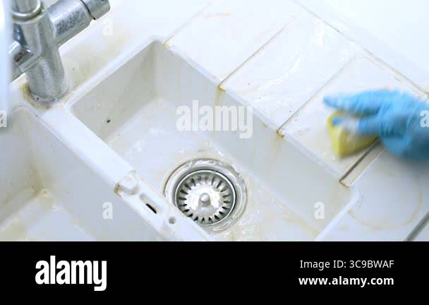Cleaning a kitchen sink with soapy water. A person with a blue glove ...