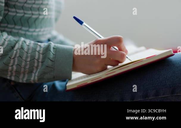 A person sits comfortably, jotting down notes in a colorful notebook ...
