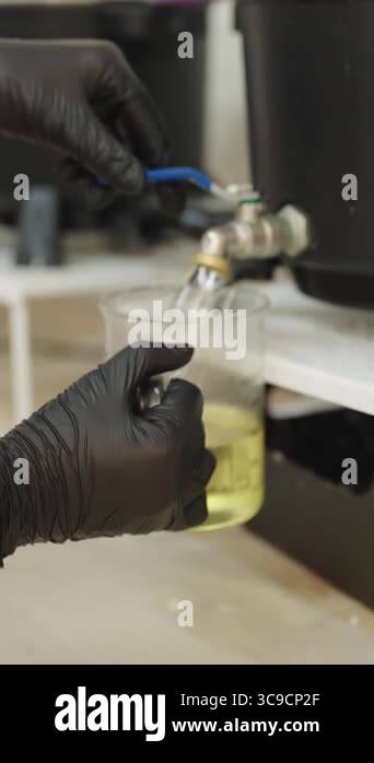 Gloved hands skillfully manipulating a faucet to fill a beaker with ...