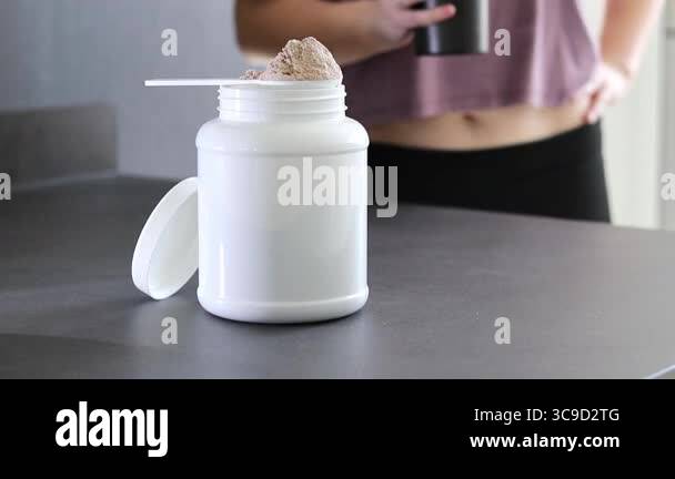 Close up of whey protein powder box and pink dumbbells on table, woman ...