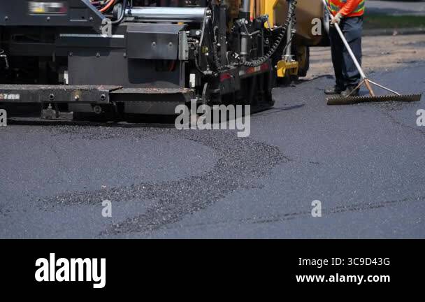 Asphalt paving machine laying fresh blacktop on a road. A worker in a ...