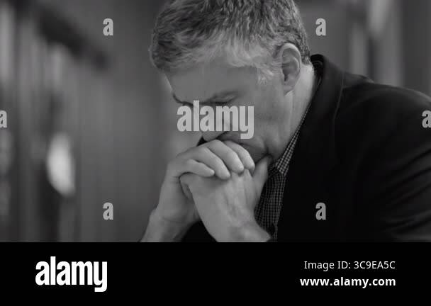 Older man bowing head with both hands clasped in front of mouth ...