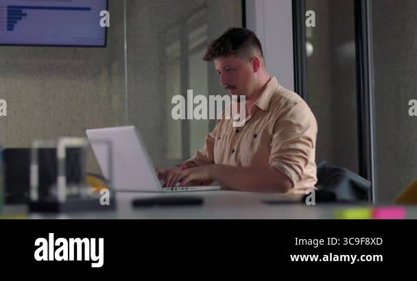 Young male employee types focused on laptop at modern office desk ...
