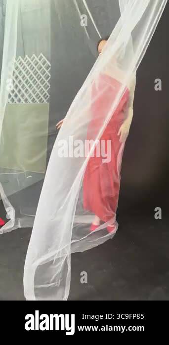 A model poses in a studio, draped in sheer fabric, creating an ethereal ...