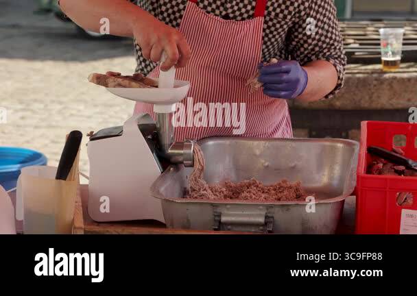 A butcher in a red striped apron uses an electric grinder to process ...