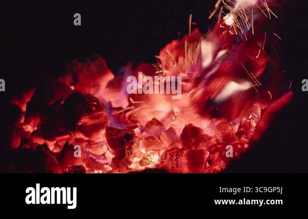 Close-up of a campfire with glowing coals at night.. A man stirs ...