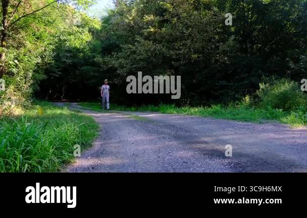 Man walking along a rural dirt road, surrounded by fields and forest, capturing the peaceful ...