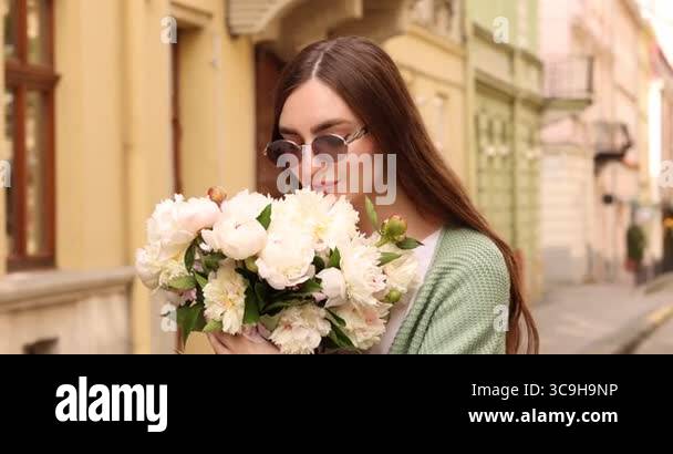 Beautiful woman smelling peonies on city street Stock Video Footage - Alamy