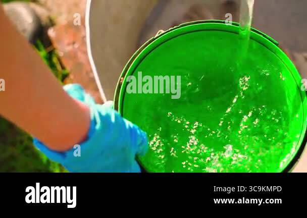 Pouring water into a green bucket close-up, top view in slow motion ...