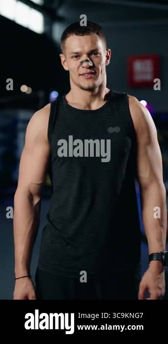 A muscular man stands in a gym, looking determined. He wears a black ...