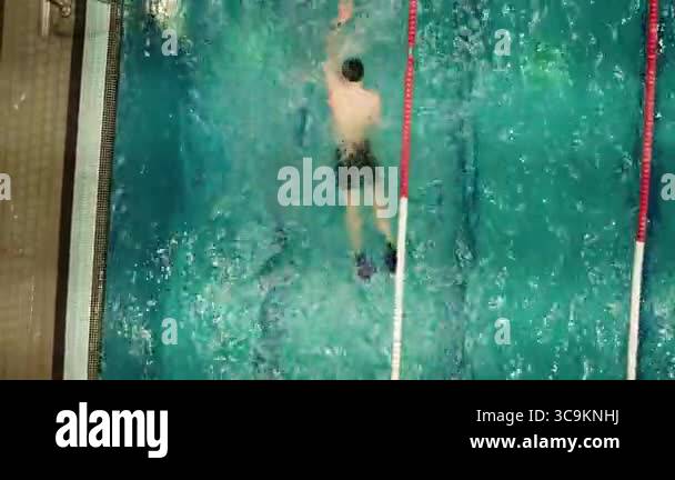 Dynamic aerial shot of a man swimming laps in an indoor pool ...
