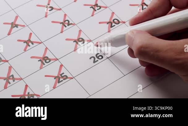 Close-up of a hand using a red marker to cross out dates on a calendar ...
