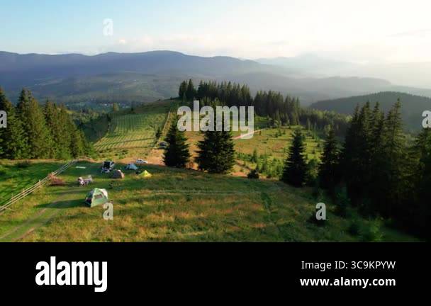 Aerial view of picturesque campsite on grassy hill, surrounded by ...
