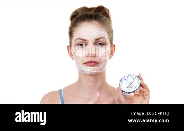Young woman applying mask moisturizing skin cream on face. Girl taking ...