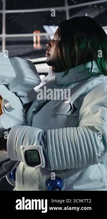 Vertical video Female astronaut in spacesuit checks wrist device inside ...