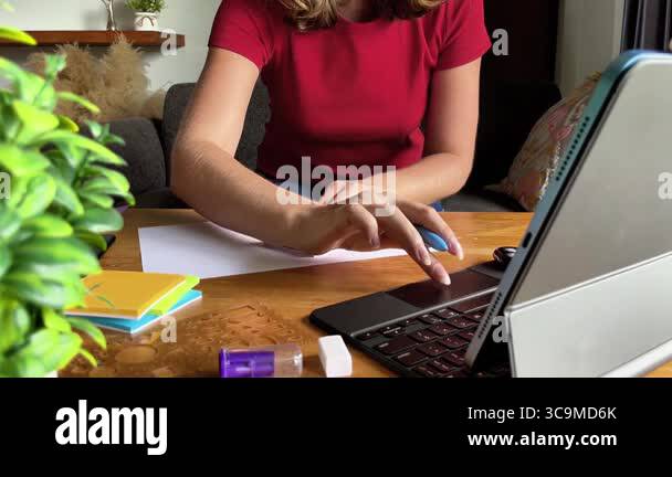 A young woman takes notes on a sticky note while working remotely on a ...