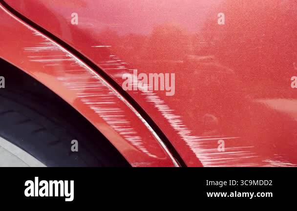 Deep scratches on red metallic car fender showing damage to paint layer ...