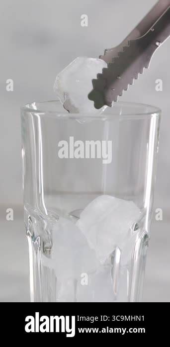 Close-Up of Stainless Steel Tongs Placing Ice Cubes into Tall Glass ...