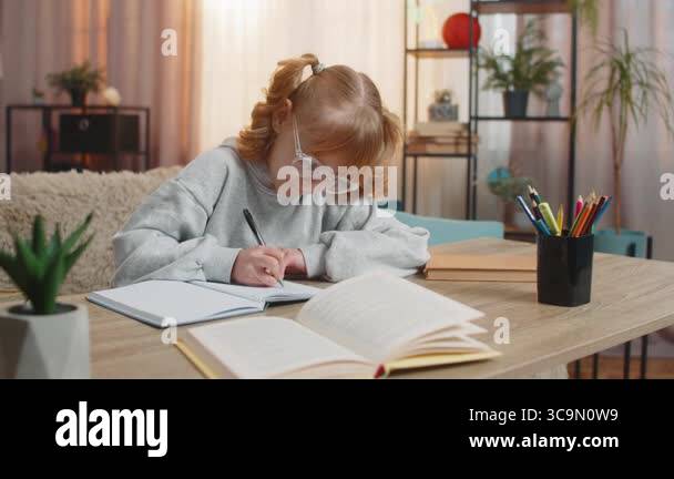 Young school girl sitting at table on sofa, focused on solving a task ...