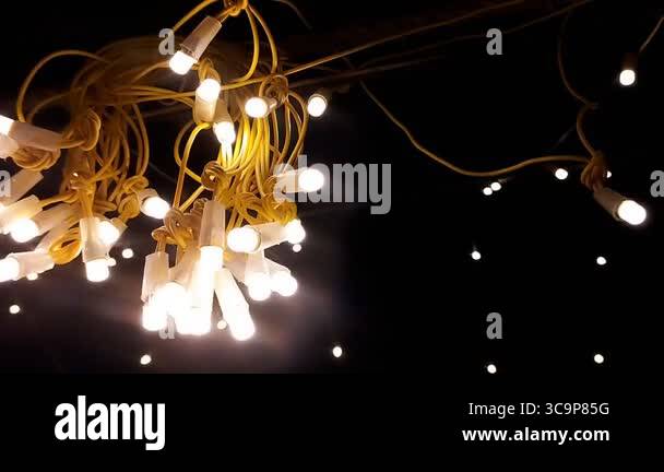 Closeup of a tangled cluster of yellow wired string lights, emitting a ...