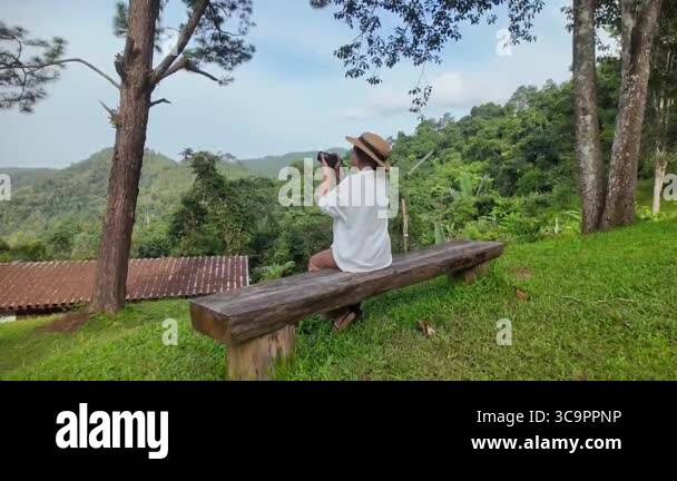 Asian female tourist is taking photos outdoors with a camera in a park ...