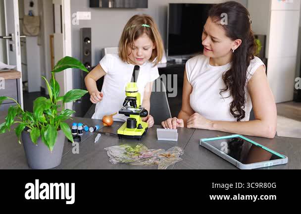 Little girl and her mother examining onion skin under a microscope at ...