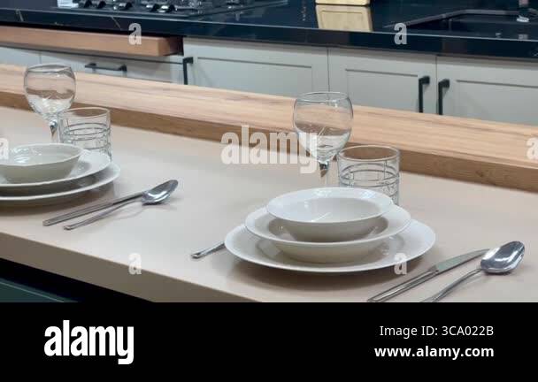 A modern kitchen counter is set with white plates, bowls, cutlery and ...