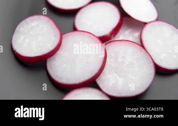 Fresh sliced radish slices falling on black ceramic plate. Raw salad ...