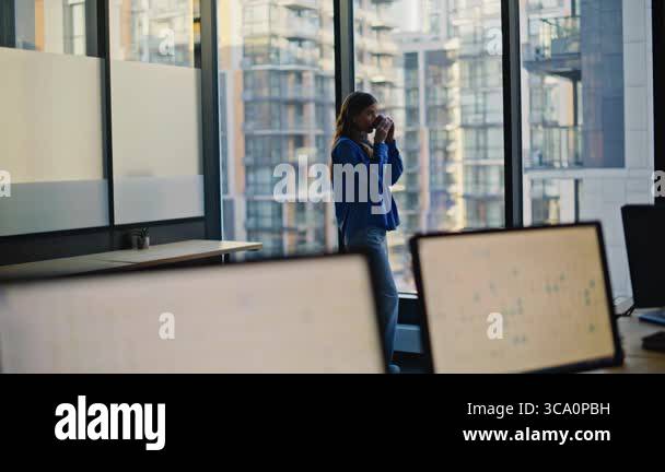 Attractive serious office manager drinking coffee standing at panoramic ...