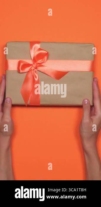 Woman holding a gift box on an orange background, presenting a surprise ...