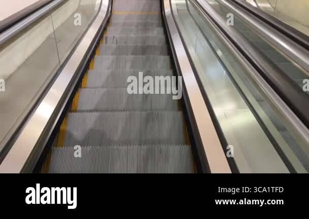 An escalator viewed from above with clear glass railings, metallic ...