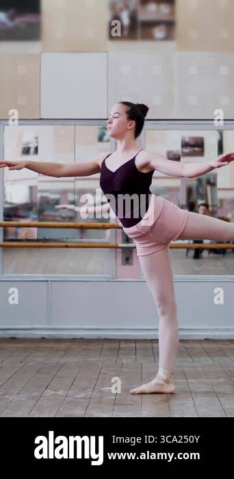 In dancing hall, Young ballerina in black leotard performs 1 arabesque ...