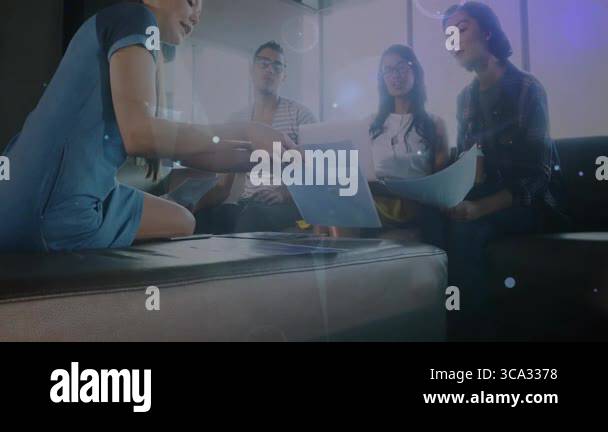 Female collaborator leaning forward handing document to team in lounge with business data ...