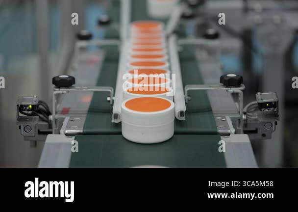 Close-up of plastic jars with orange lids moving in a line on an ...