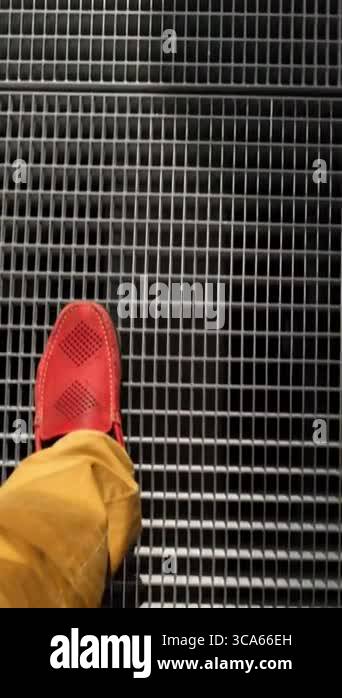 A single red shoe steps onto a textured metal grid walkway, portraying ...
