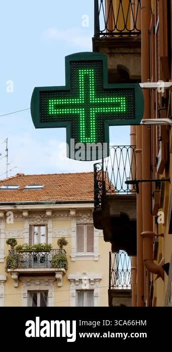 A vibrant green pharmacy cross sign stands out against an urban ...