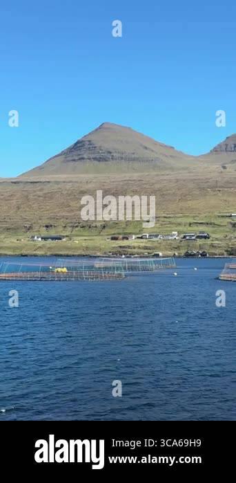 Open-net salmon cages float in a Faroese fjord, Faroe Islands, beneath ...
