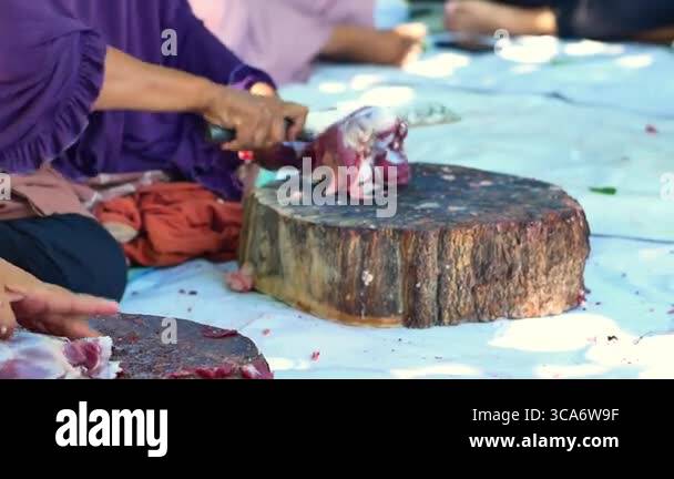 A group of women are cutting a pile of goat meat on a wooden tray with ...