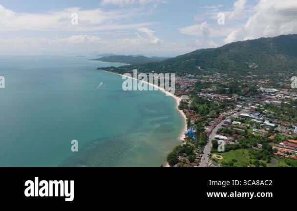 Wide stretch of beach with clear turquoise sea and green tropical hills ...