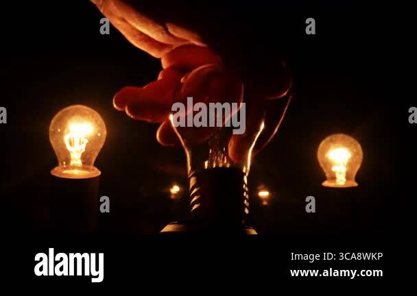 Close up of a hand unscrewing an old incandescent bulb and screwing in ...