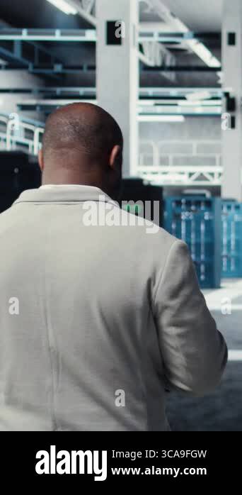 Vertical video Admin walking in high tech data center facility, checking equipment for system ...