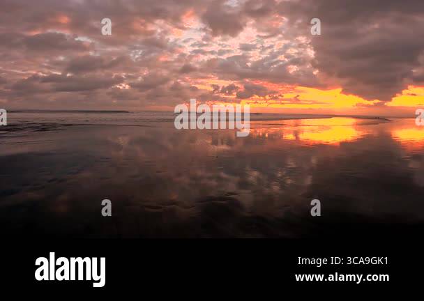 Kuta Beach at sunset with clouds reflecting on wet sand and sea water ...