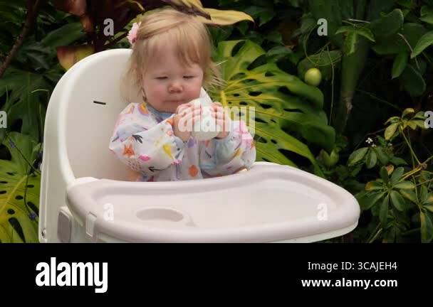Cute toddler learning to sit on a plastic chair in a lush tropical ...