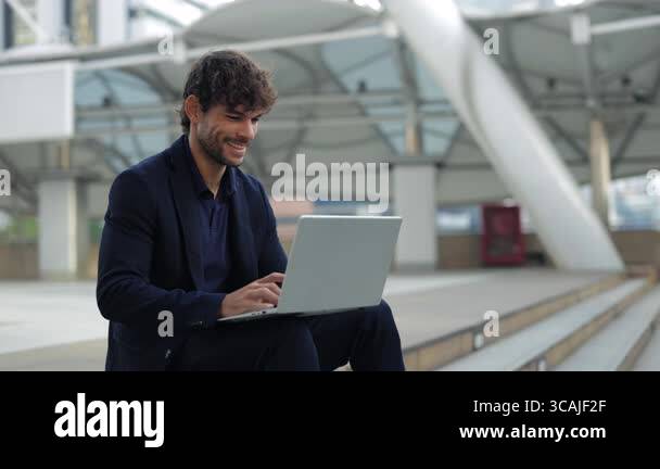 Portrait of Hispanic office worker smiles and uses laptop sitting on ...
