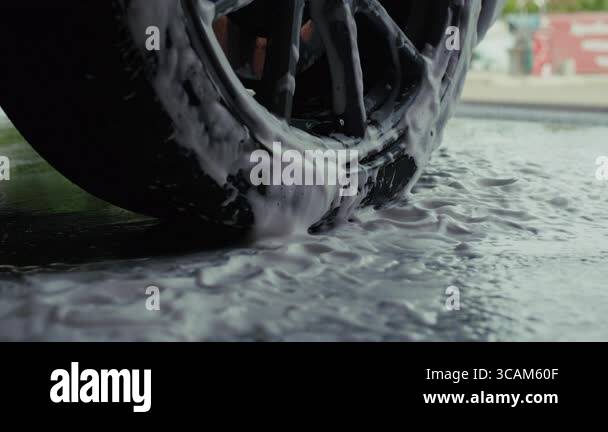 A close-up shot of a car wheel coated in thick, soapy foam during an ...
