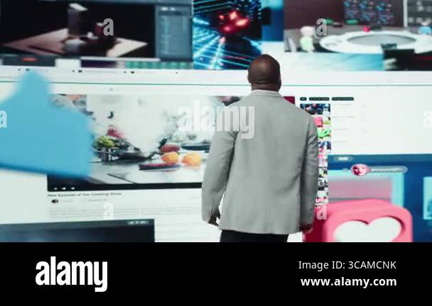 Man stands in front of digital videowall surrounded by streaming videos ...