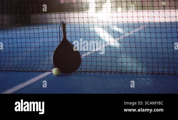 Padel racket and ball resting against net on blue court, copy space ...