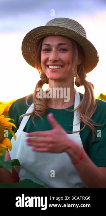 Farmer stands in a vibrant sunflower field, wearing a straw hat and ...